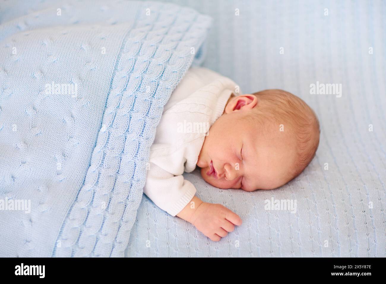 Newborn baby boy in bed. New born child sleeping under a blue knitted ...