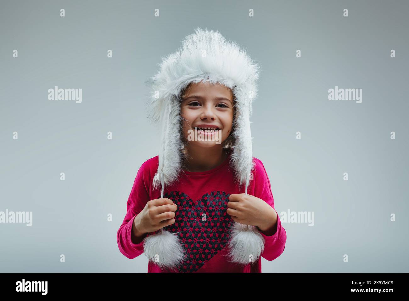 Young girl with a broad smile wears a festive white fur hat and a ...