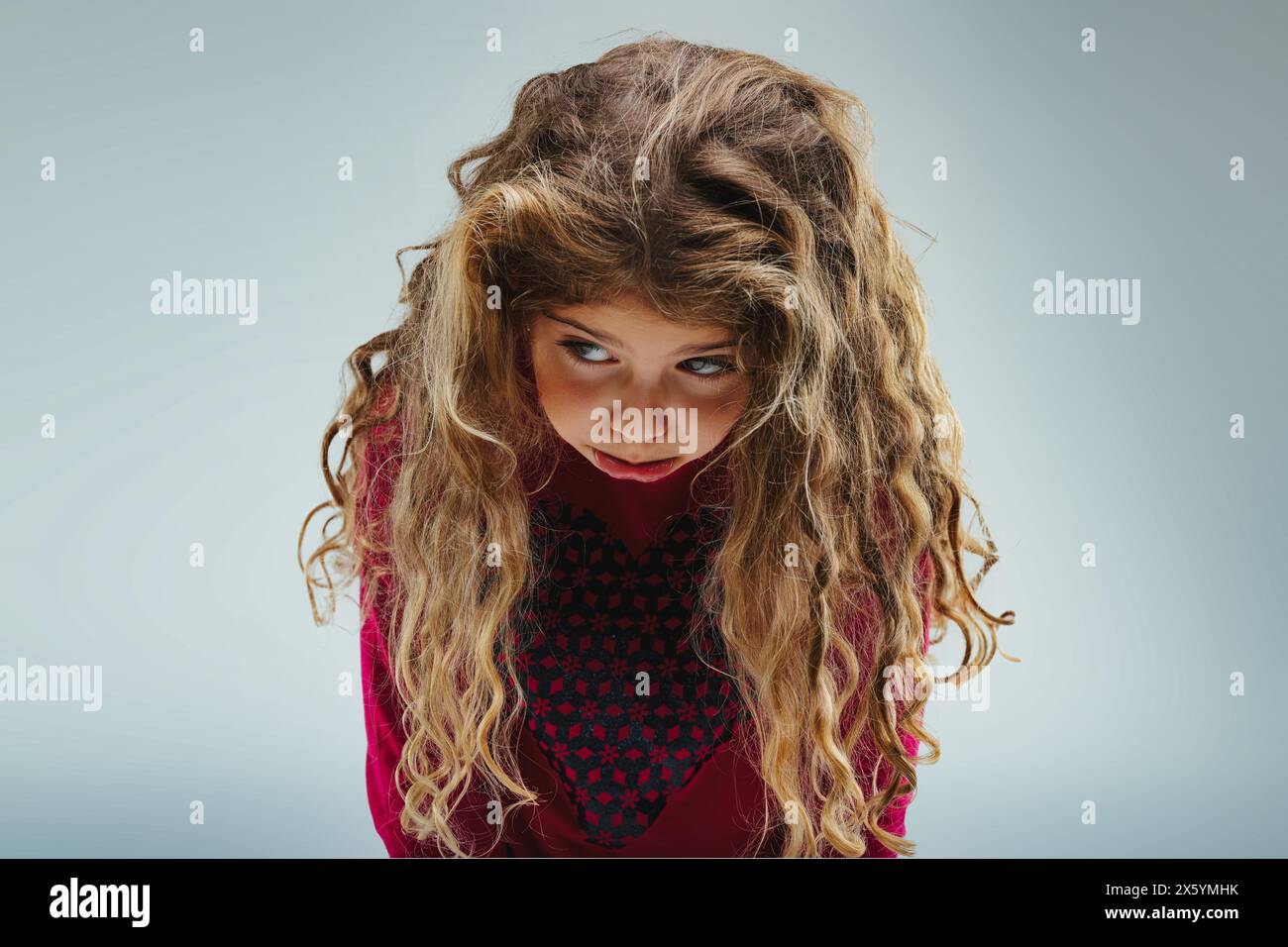 Downcast young girl with wavy blonde hair shows a somber expression ...