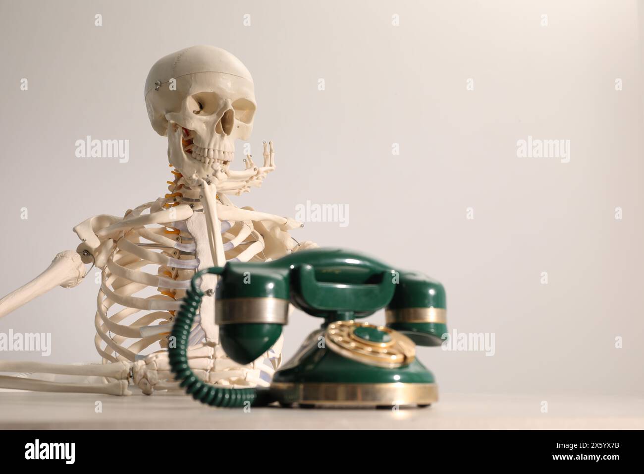 Waiting concept. Human skeleton at table with corded telephone against ...