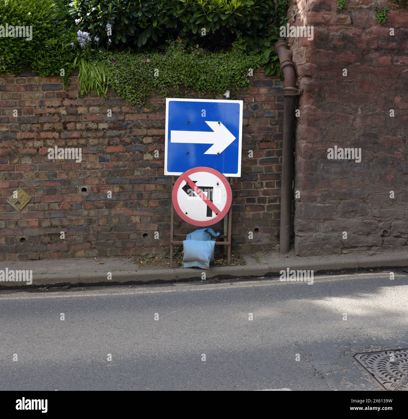 Two road signs leaning against wall at side of street Stock Photo - Alamy