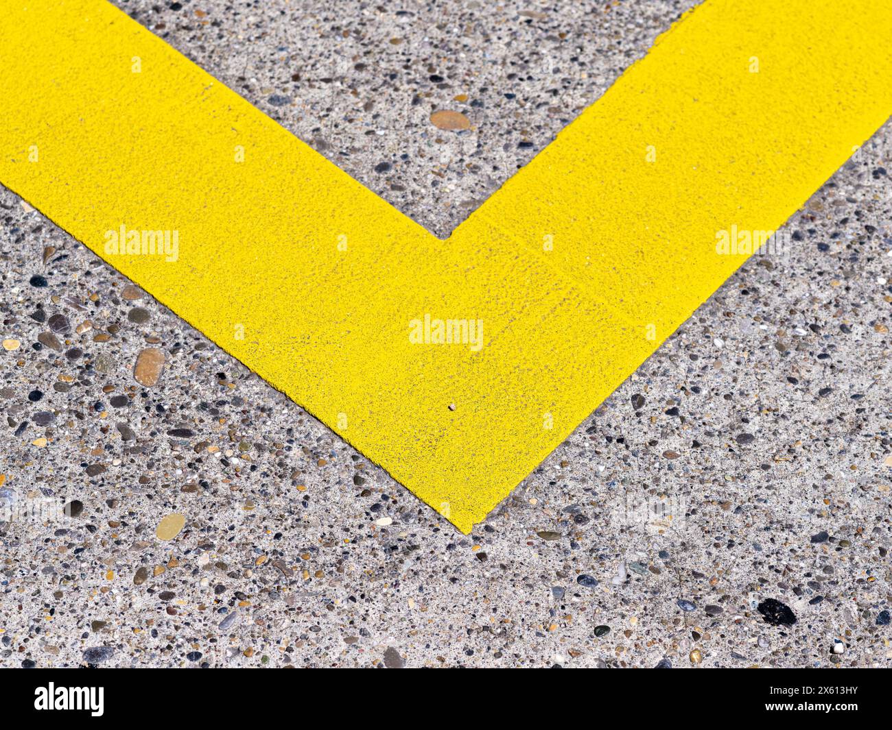 Close-up view of yellow V-shaped line on textured concrete pavement ...