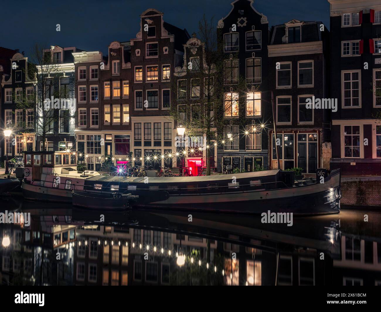An illuminated houseboat reflecting in the Singel canal in Amsterdam at ...