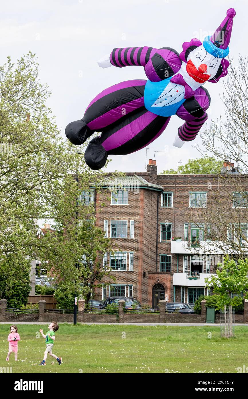 London, UK. 12 May 2024. Children pass beneath a giant clown kite flown ...