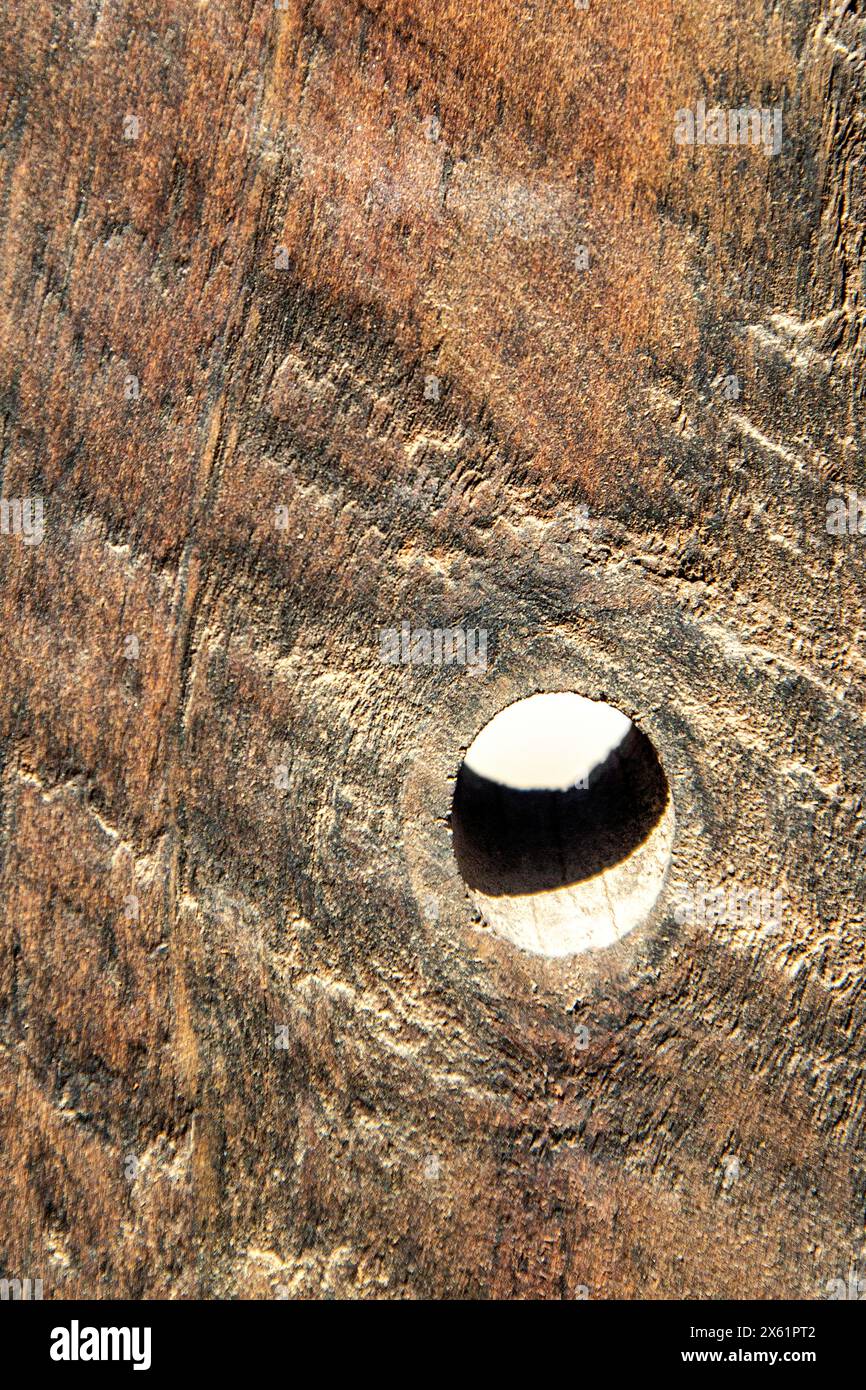 A knot hole through a brown, orange and grey, wooden, diagonally ...