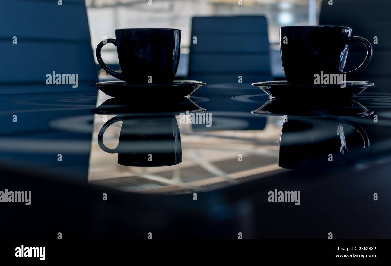 Black cups for tea or coffee on black glass table with reflections on ...