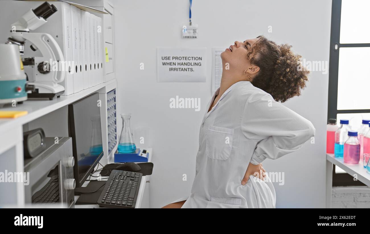 A young woman with curly hair wearing a white lab coat stretches her ...