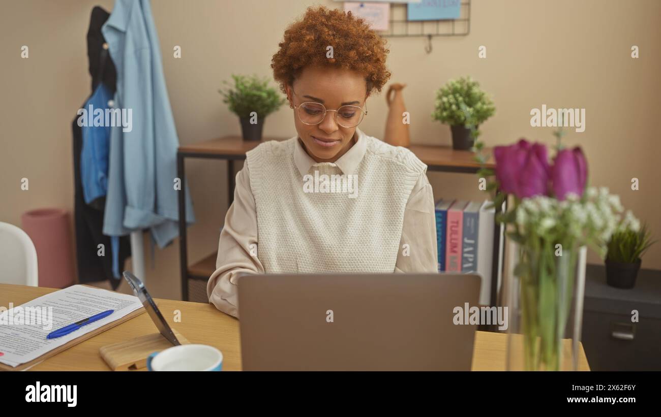 Focused african american woman using laptop in a cozy home office setup ...