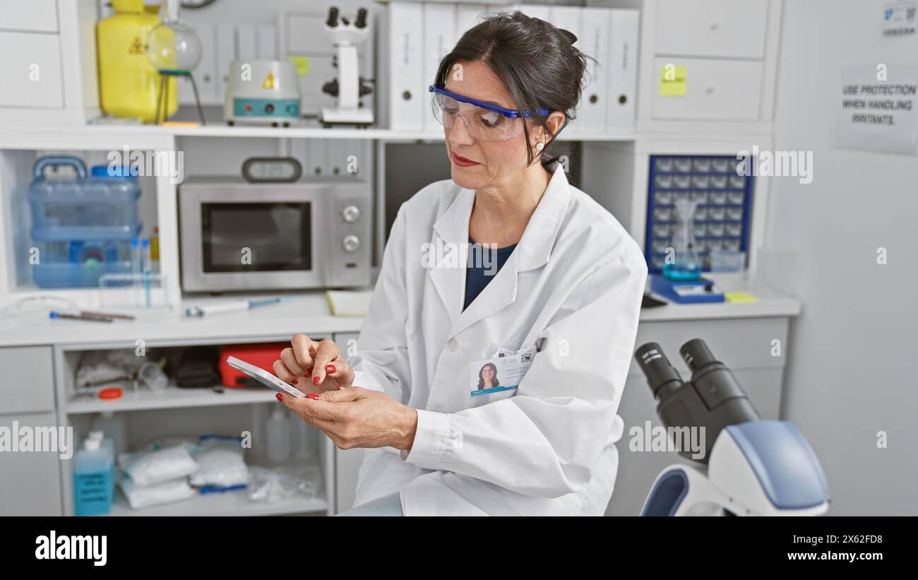 Hispanic woman scientist using smartphone in laboratory setting, likely ...