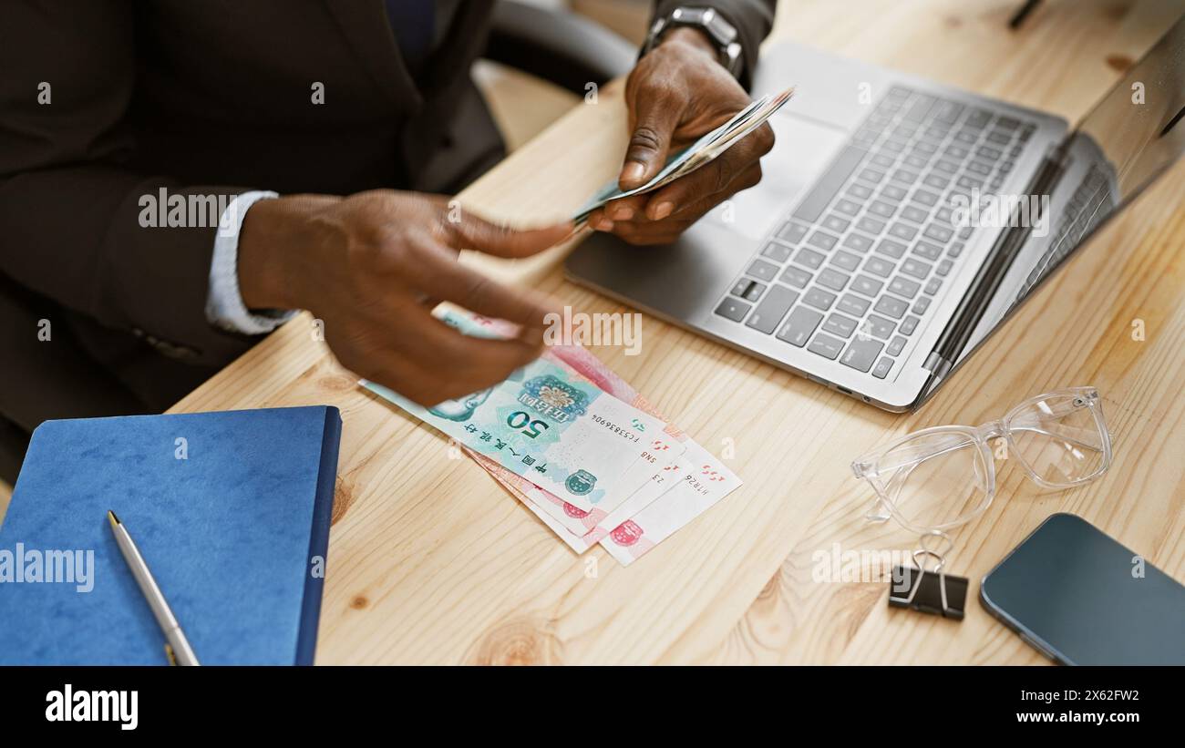 African businessman counting currency in an office setting with laptop ...