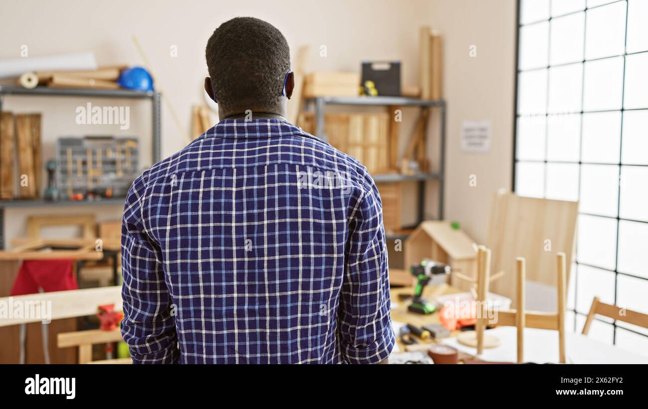 Back view of a thoughtful african man standing in a busy carpentry ...