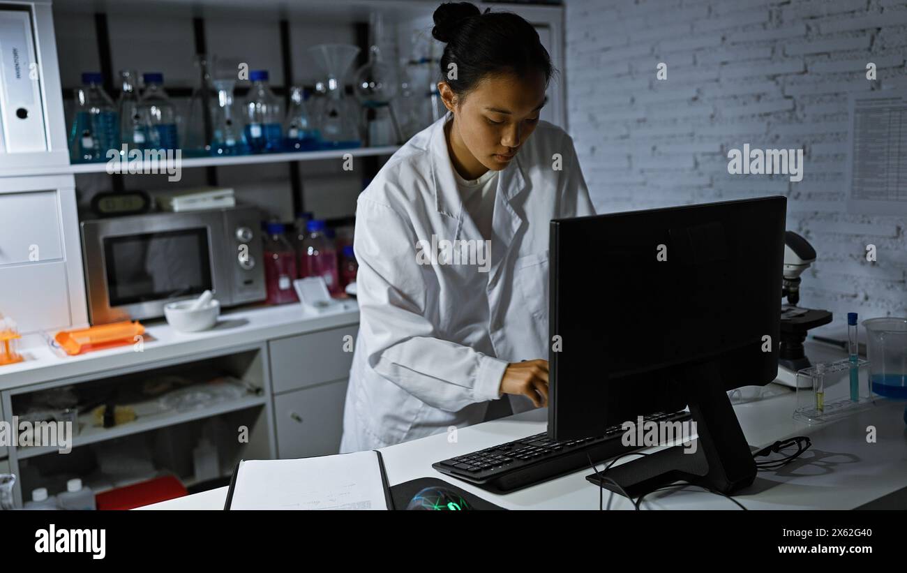 Focused chinese woman scientist using computer in a dimly lit laboratory setting, showcases ...
