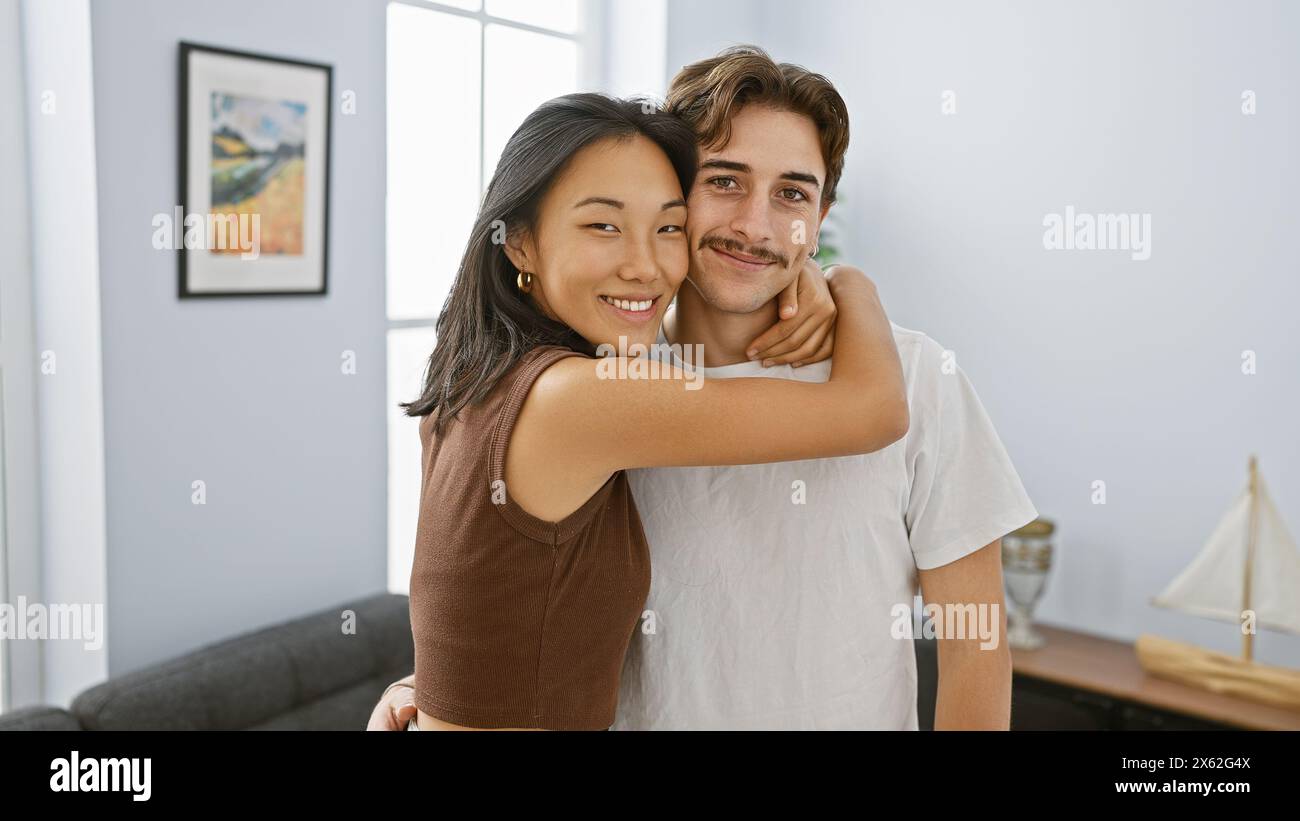 An interracial couple hugs lovingly in a cozy living room, showcasing harmony and affection ...