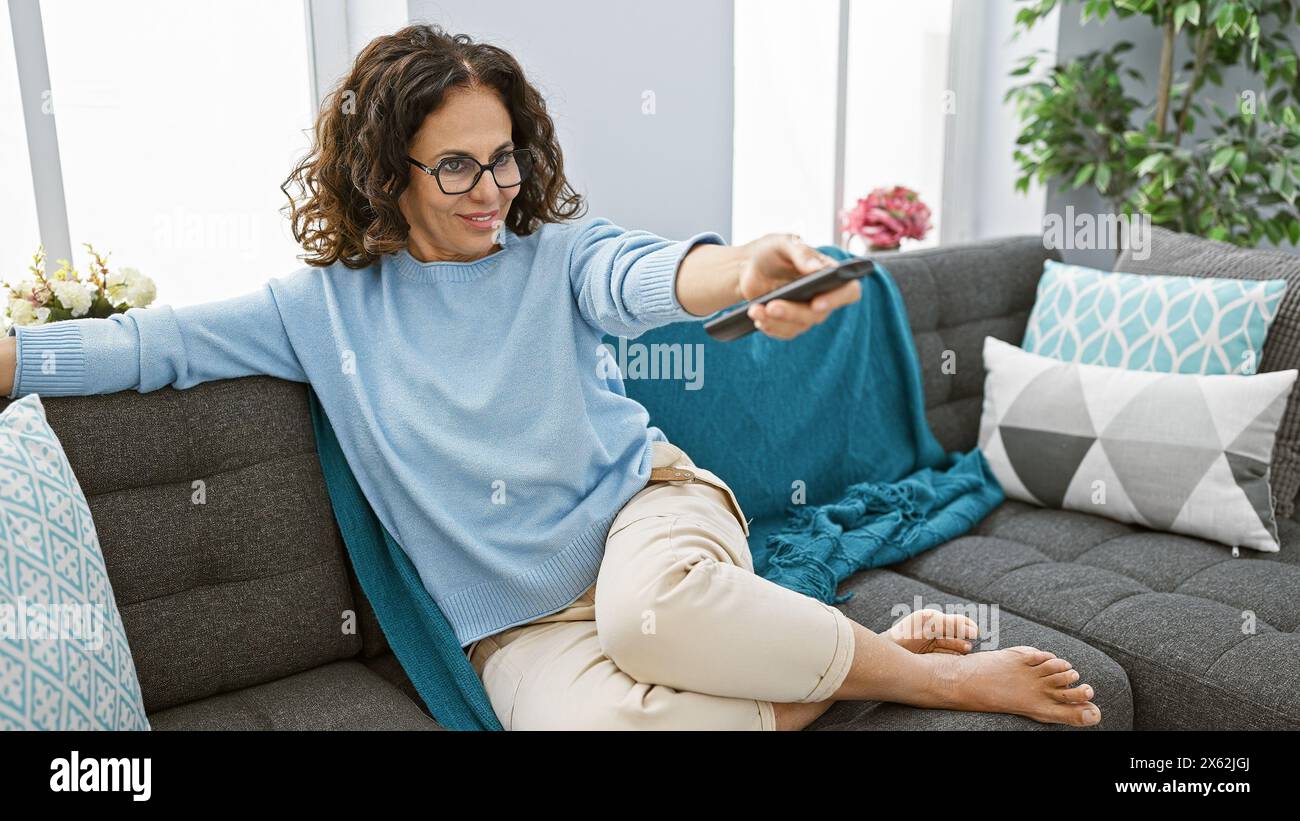 A middle-aged woman with curly hair comfortably relaxes at home ...