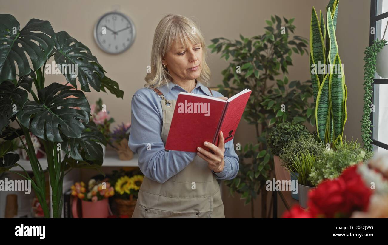 Blonde woman reading red book in lush flower shop interior with plants ...