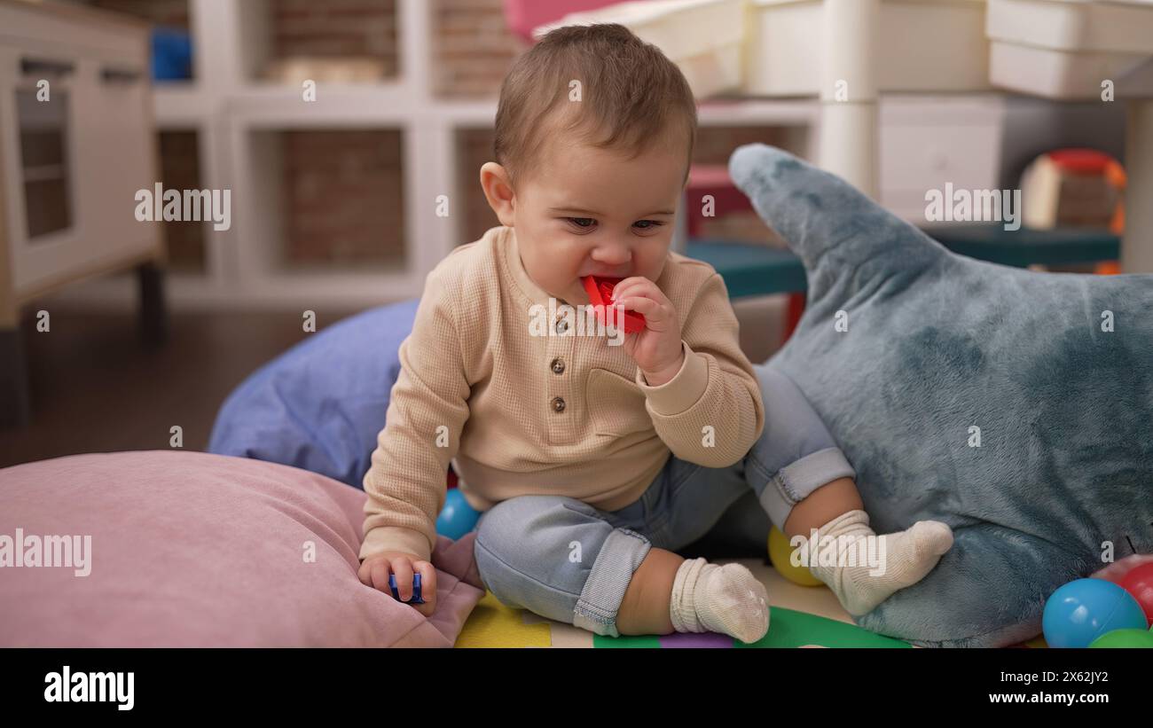 Adorable toddler bitting plastic construction blocks sitting on floor ...