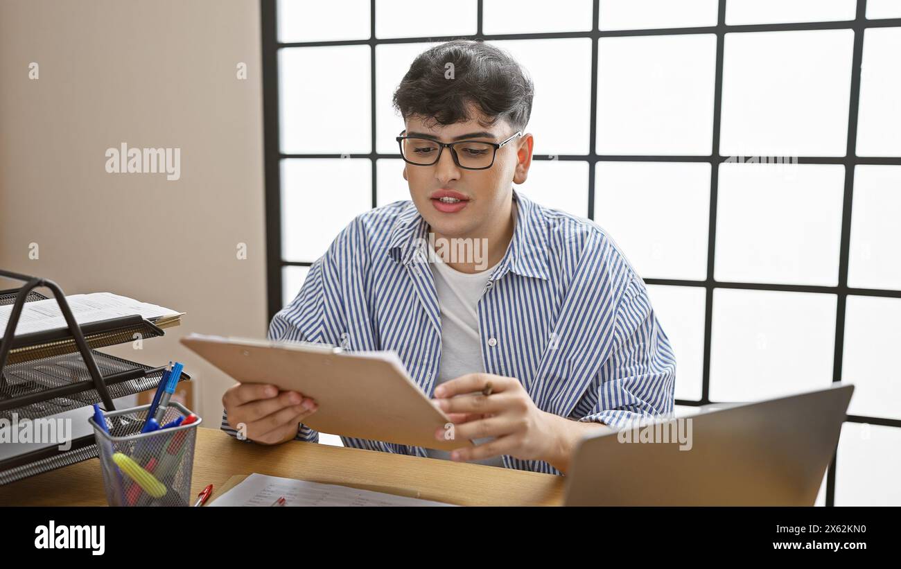A young man in glasses works diligently in a modern office, reviewing ...