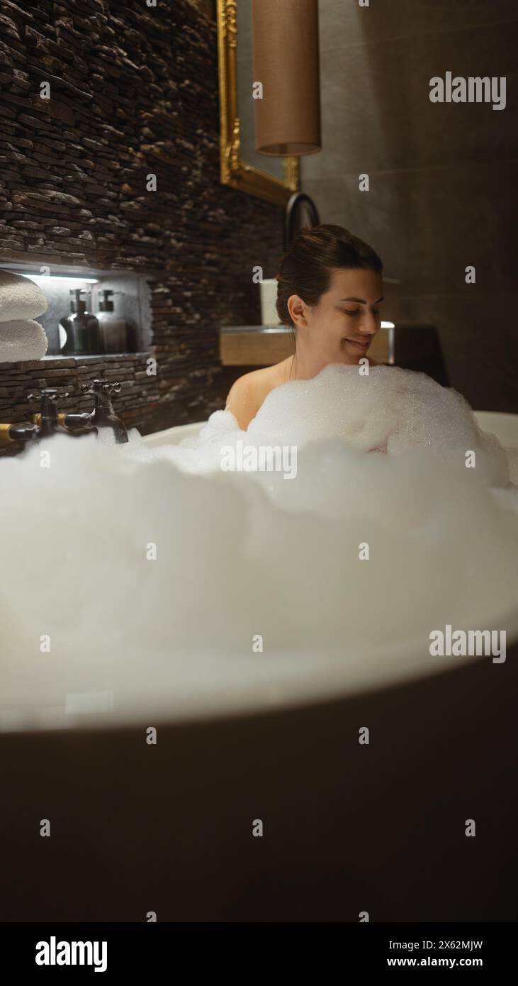 A serene young woman enjoys a luxurious bubble bath in a modernly designed bathroom Stock Photo ...