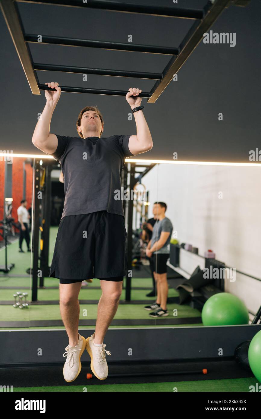 Vertical shot of beginner sportsman doing pull-ups on horizontal bar at ...