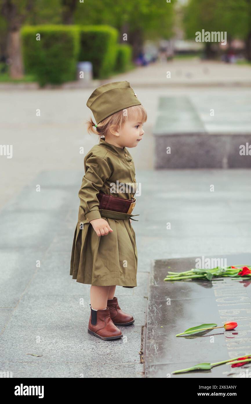 Adorable baby in Soviet military uniform lays a flower on a monument ...