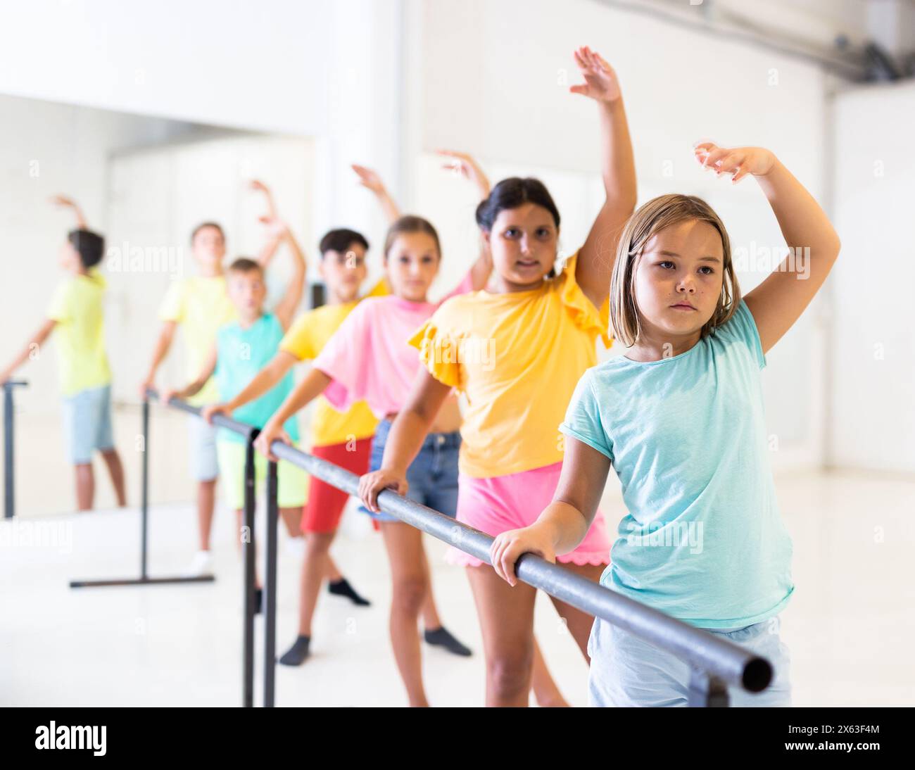 Focused tween girl practicing ballet positions near bar during group ...