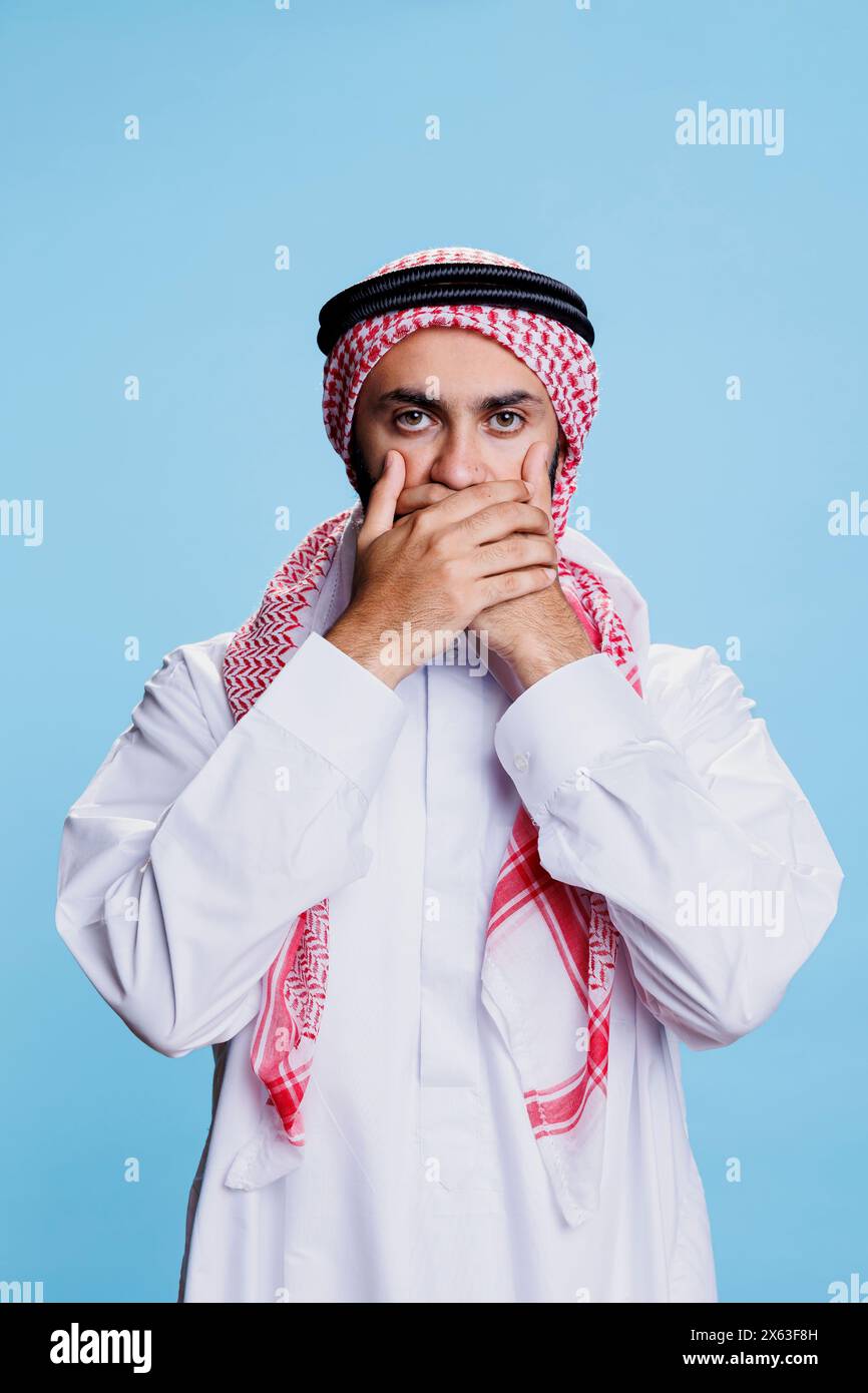 Arab man wearing traditional islamic clothes holding palms on mouth and ...