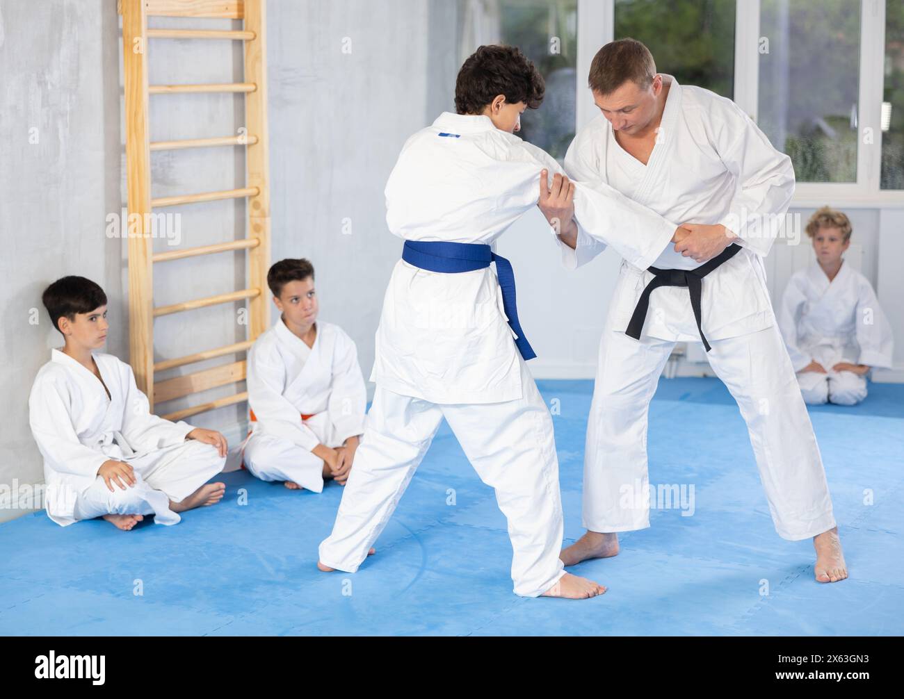 Male karate instructor training little child wearing kimono in dojo or ...