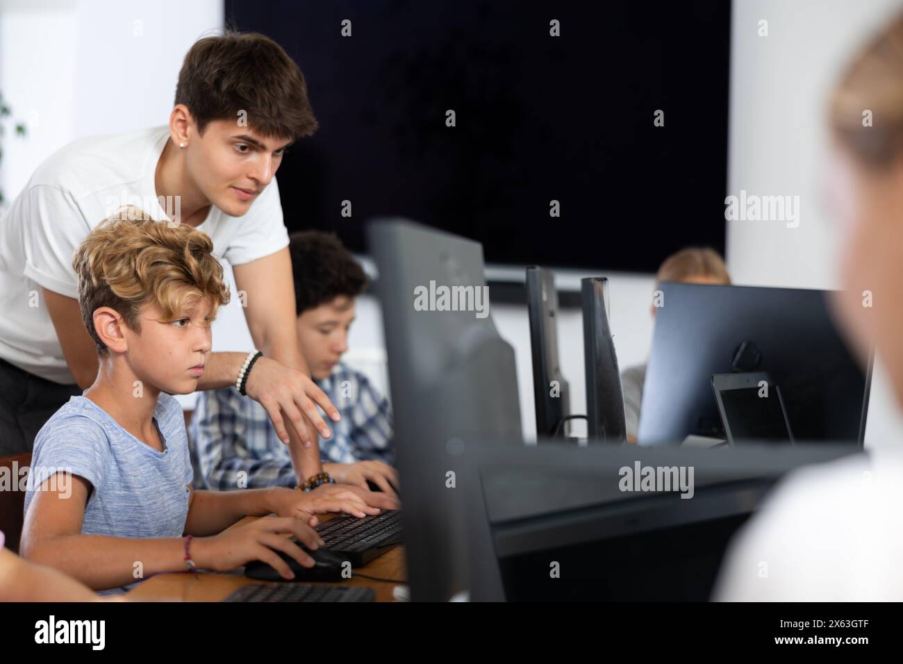Preteen boy learning computer programs with teacher in training room ...