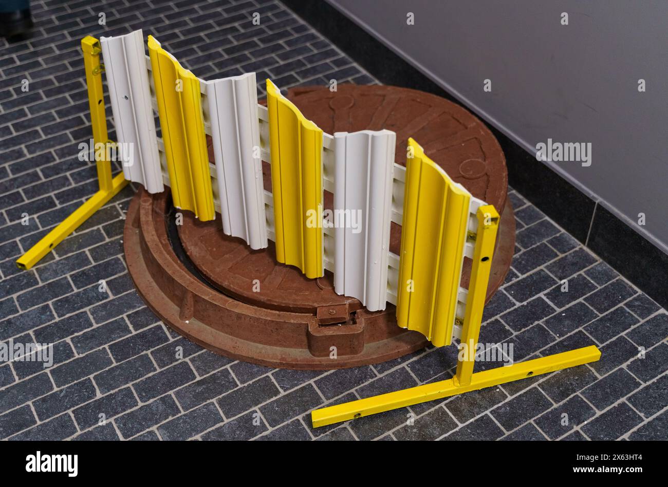 A bright yellow foldable safety fence surrounds an open brown well ...