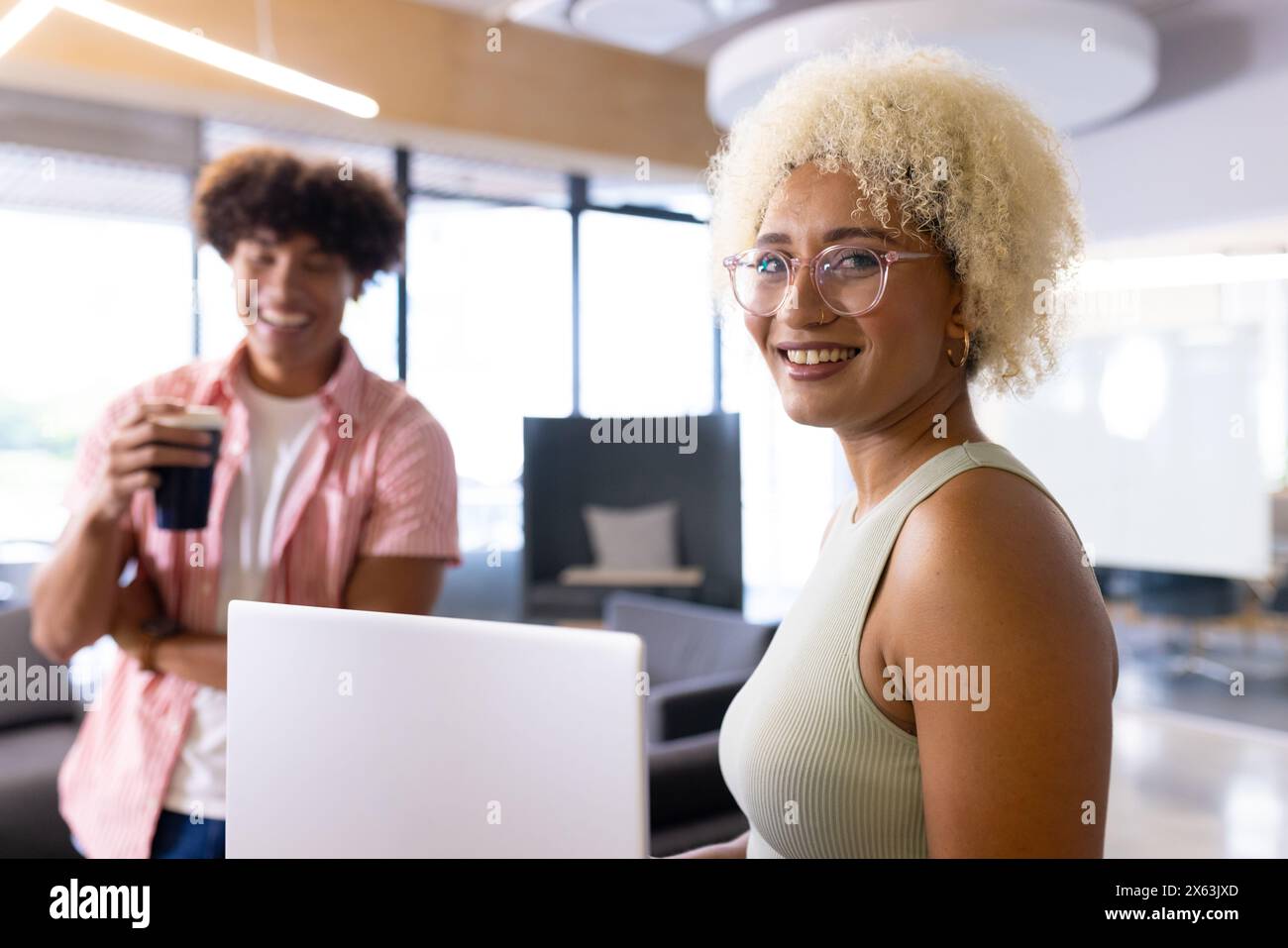 In modern office, two biracial coworkers holding coffee, laughing ...