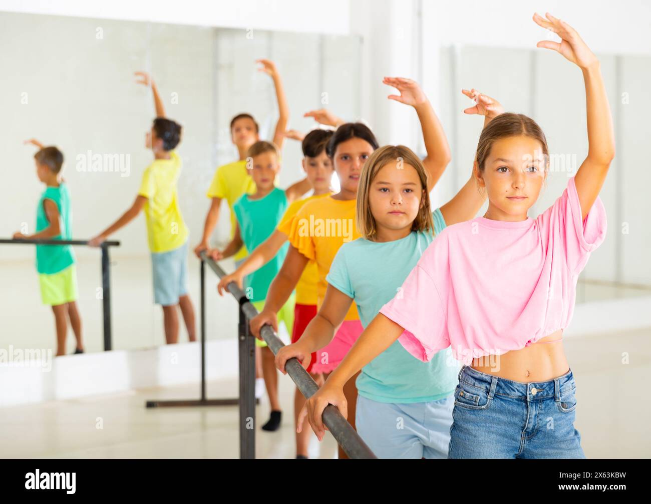 Focused tween girl practicing ballet positions near bar during group ...