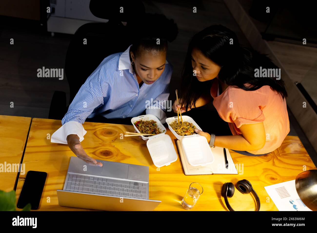 At office, diverse female colleagues eating, working late together ...