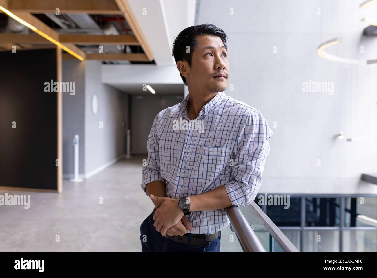 Asian male professional leaning on railing at office, looking ...