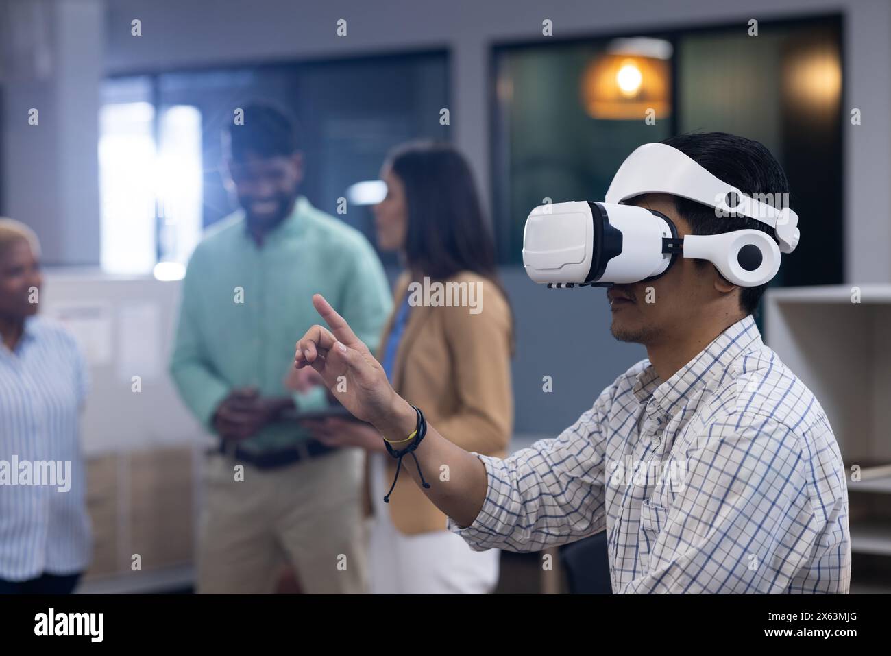 At office, Asian man wearing VR headset pointing, surrounded by a team ...