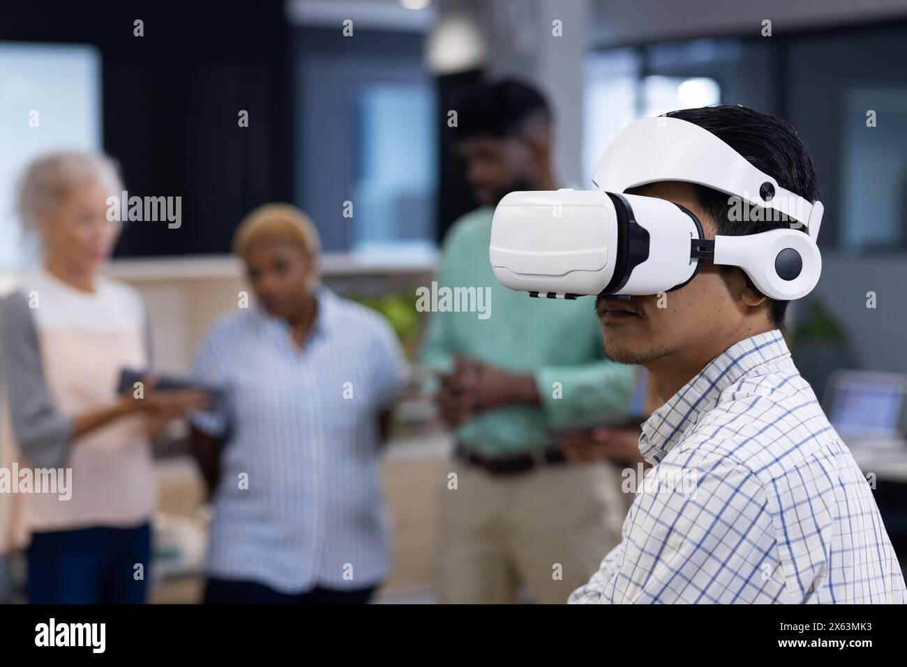 Diverse team at office observing Asian male wearing virtual reality ...
