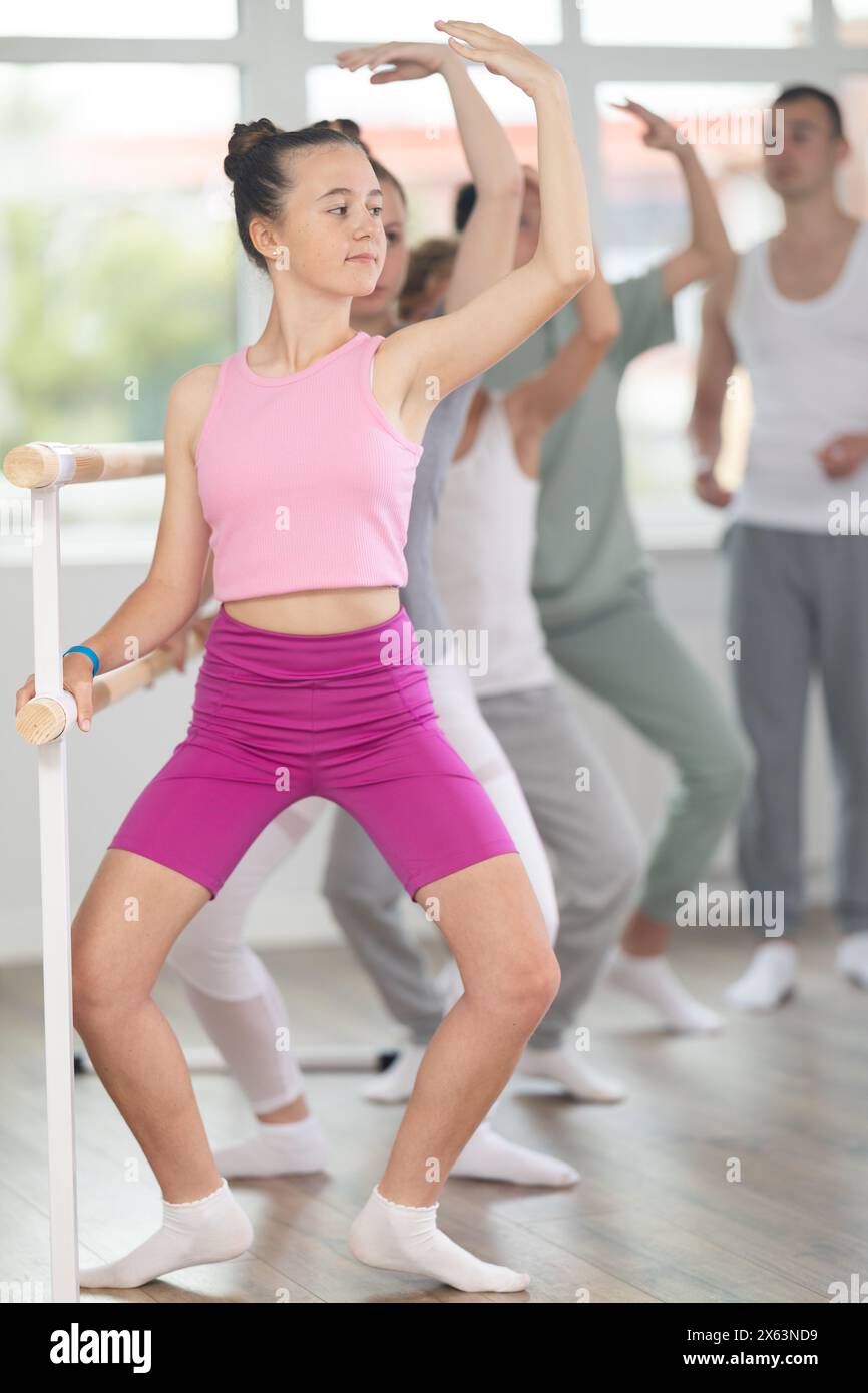 Girl doing plie exercise in class with teens in ballet studio under ...