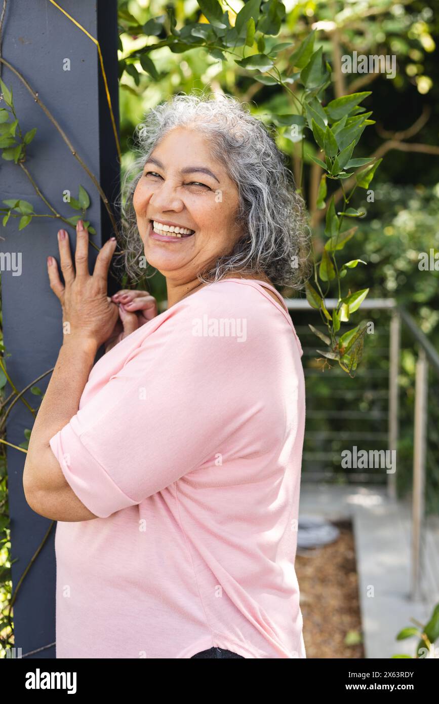 Senior biracial woman leaning against post, smiling outdoors Stock ...