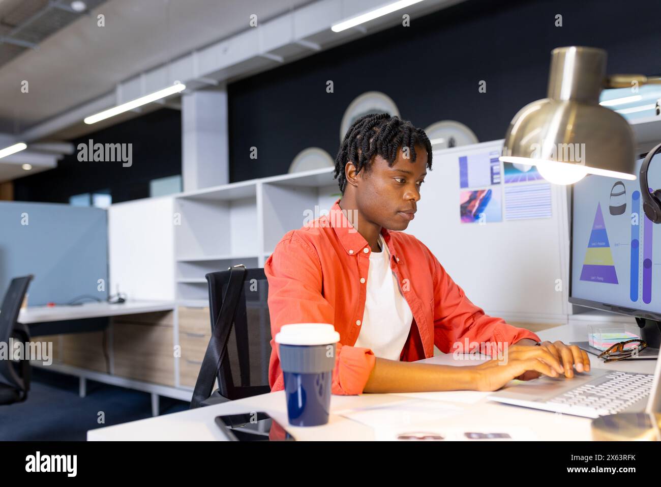 African American male manager in red shirt types on a computer in a ...