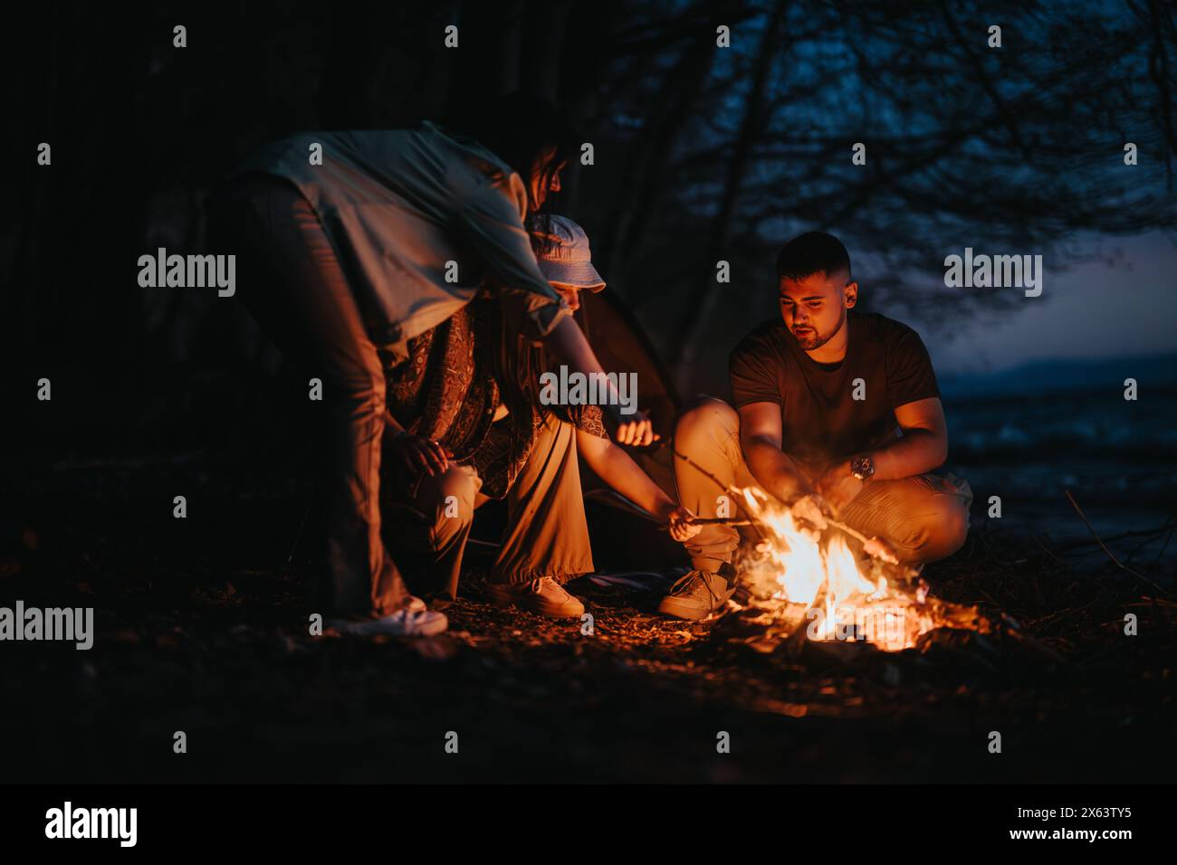 Friends enjoying a campfire dinner at lakeside during nightfall Stock ...