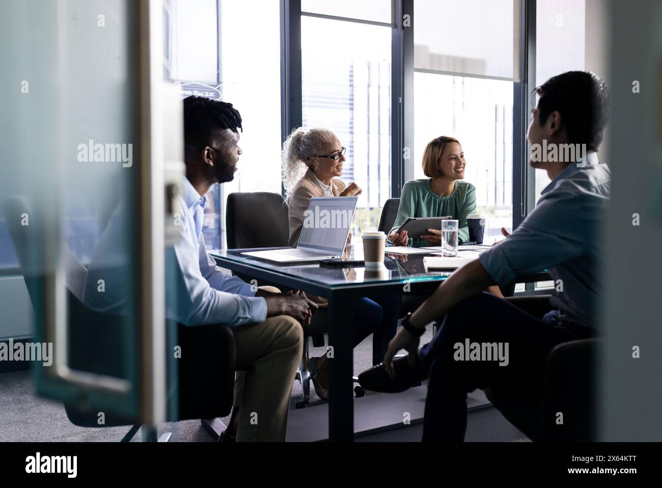 Diverse team gathering around table with a laptop at office Stock Photo ...