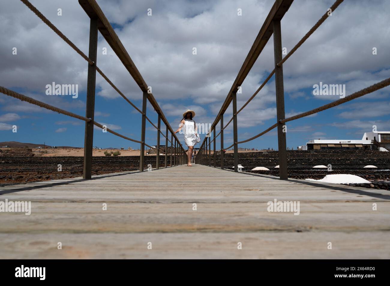 A woman is walking on a bridge with a hat on. The bridge is wooden and ...