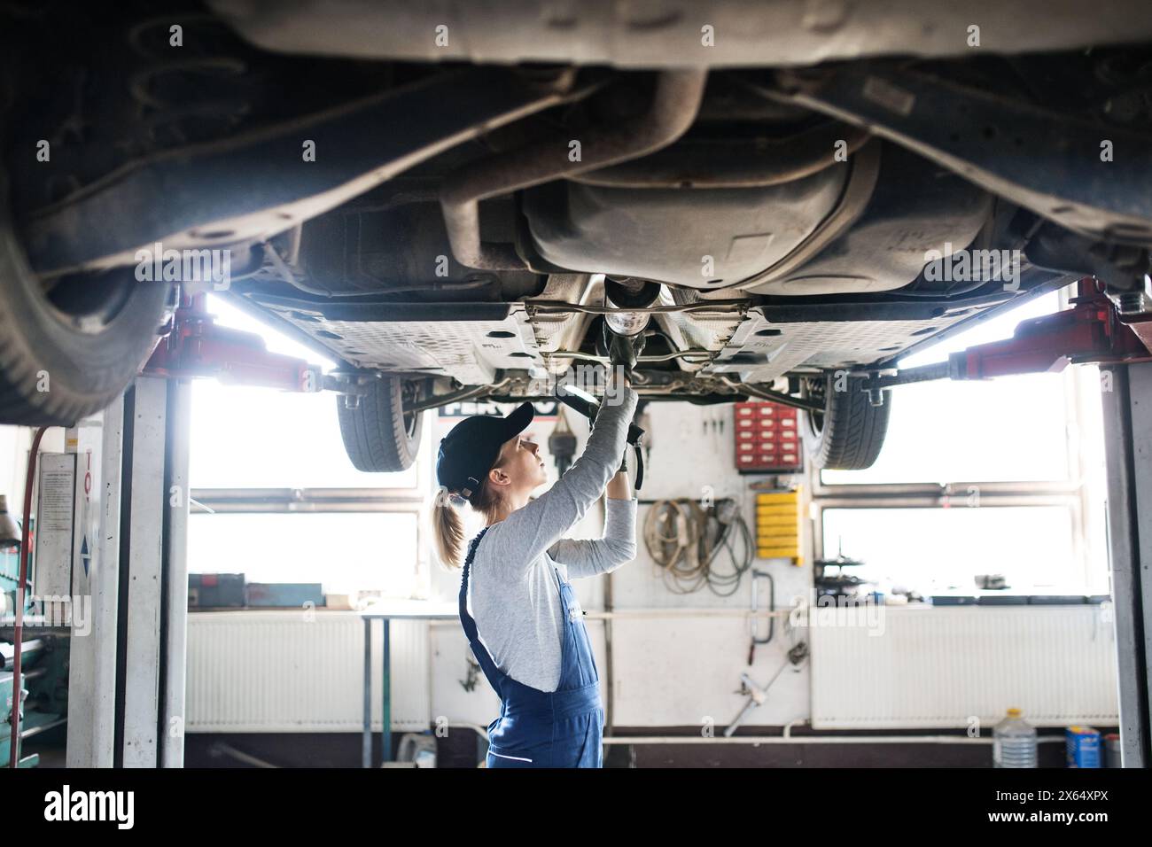 Female auto mechanic elevating car on car lift, working underneath ...