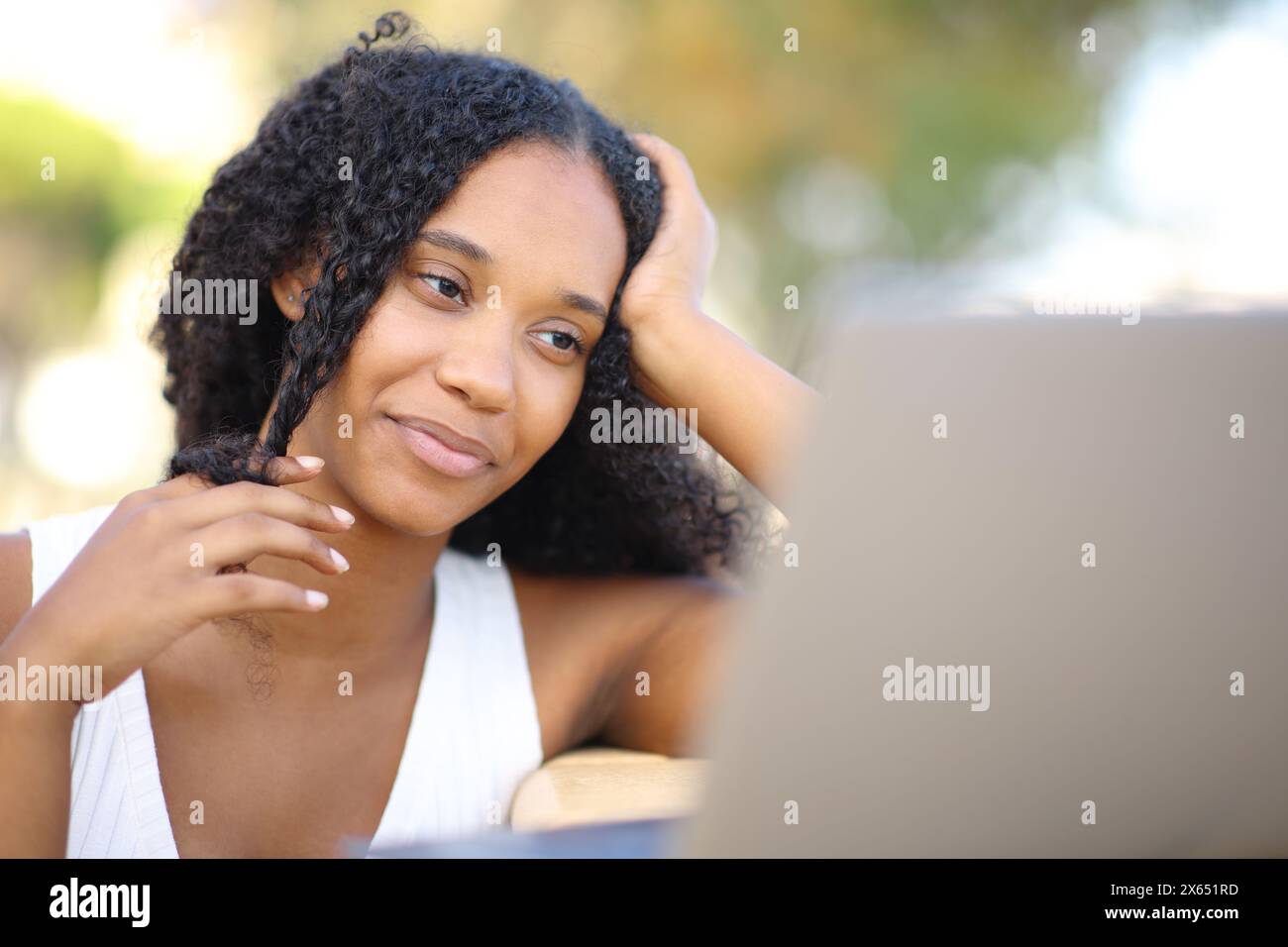 Black woman touching hair flirting while watching content on laptop ...