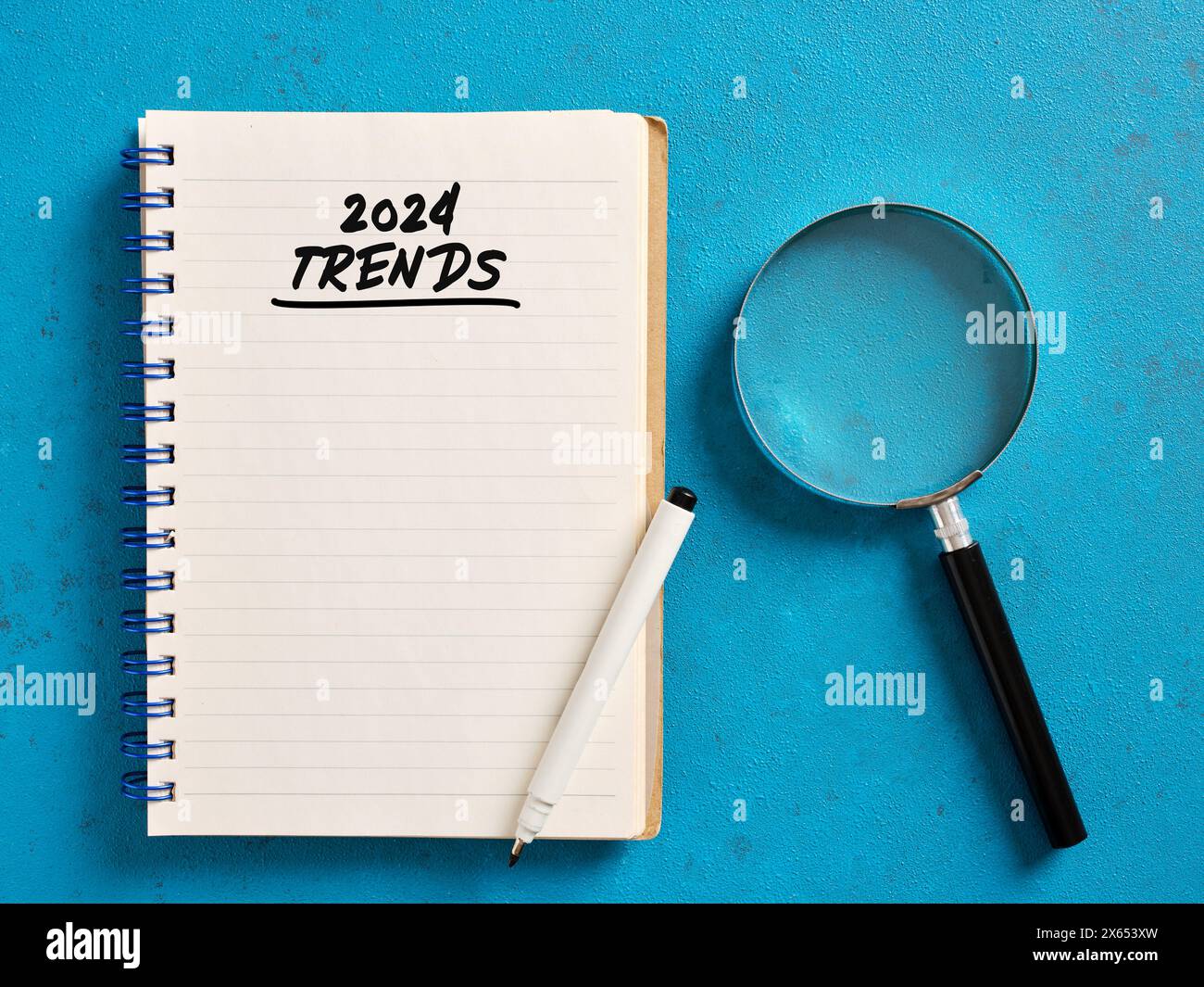 2024 trends handwritten on a notebook with a magnifier. Popular topics ...