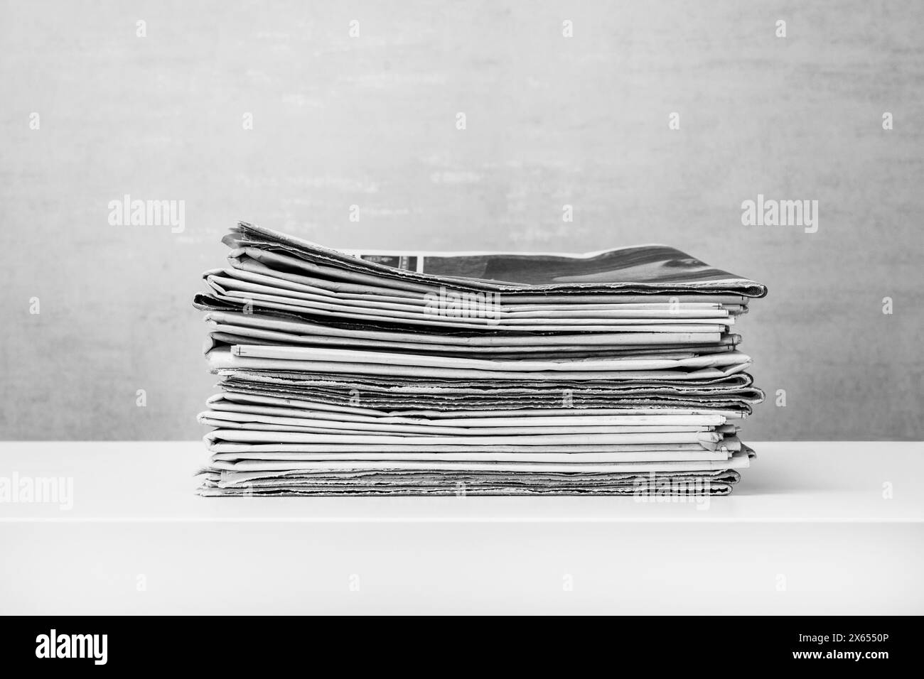 a stack of newspapers on a white table on a grey background, black and ...