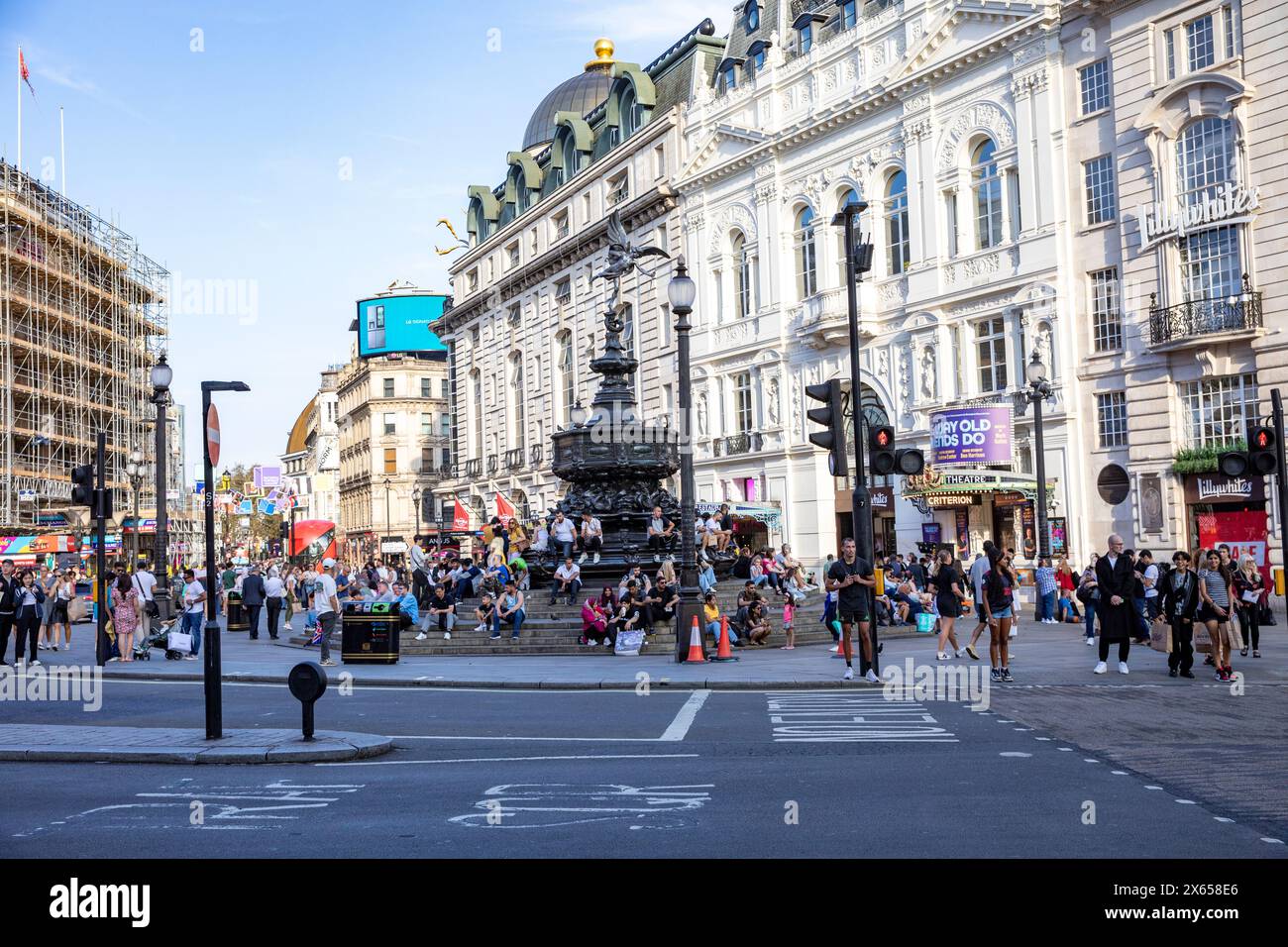 Visitors and tourists in Piccadilly Circus London West End, sitting beside statue of Eros in ...