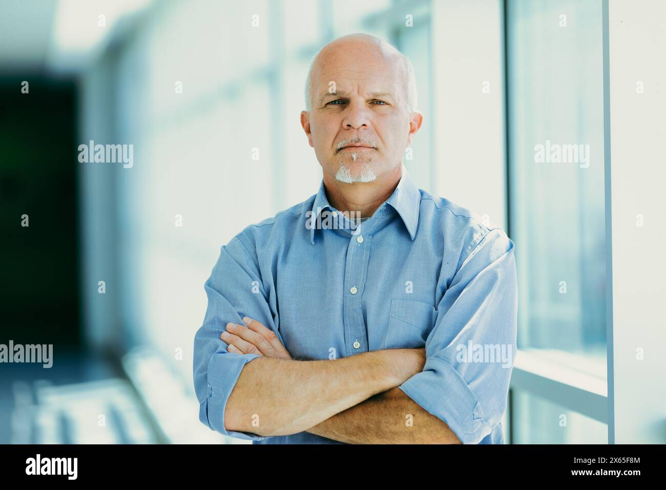 Office setting frames a serene-looking older man in blue, arms crossed ...