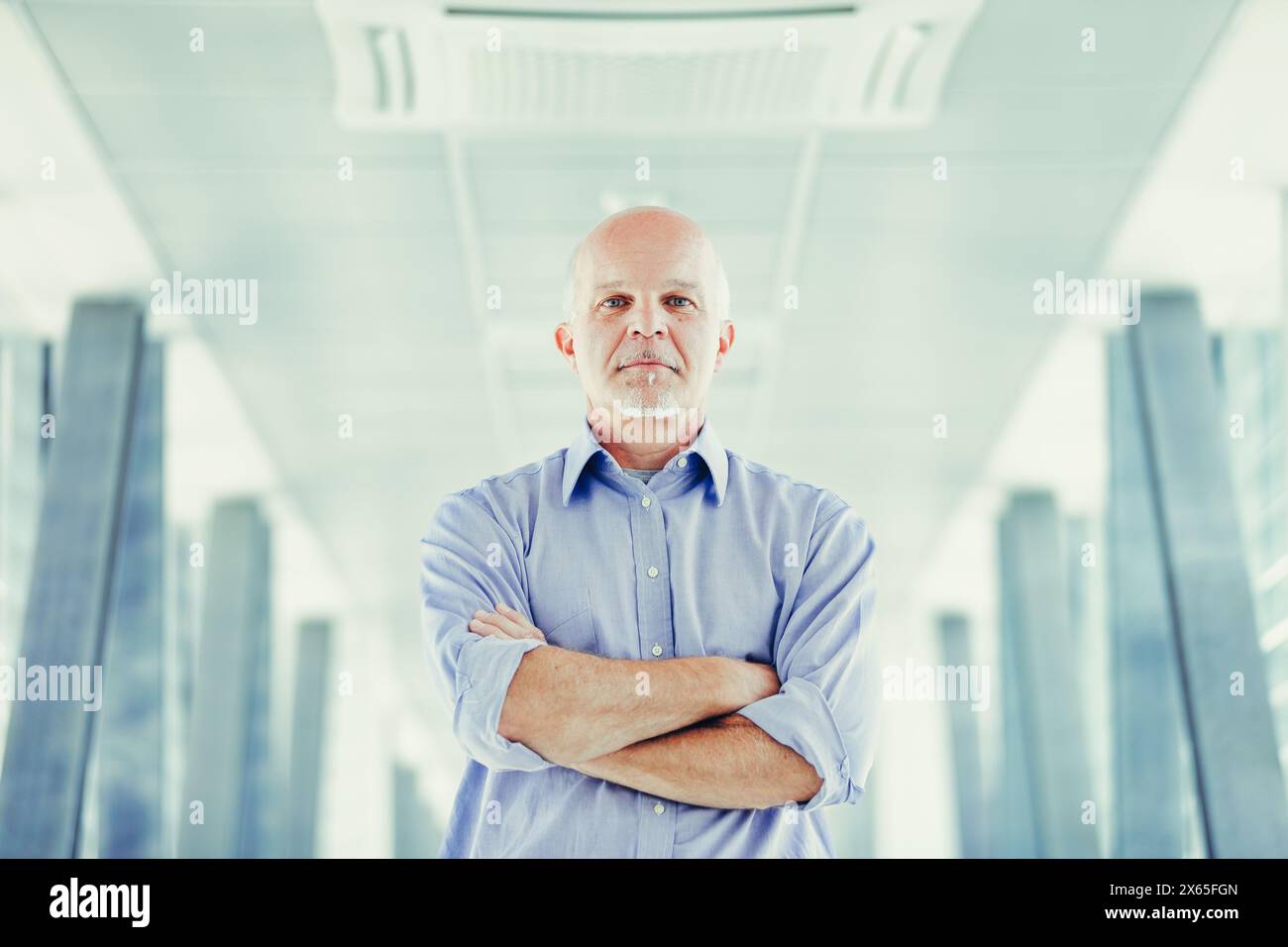 Confident older gentleman, arms crossed, wearing a casual blue shirt ...