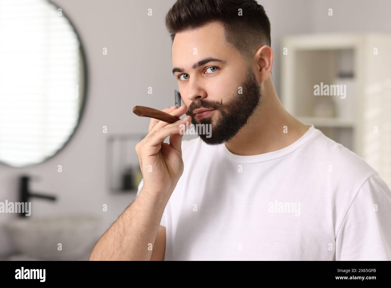 Handsome young man shaving beard with blade indoors Stock Photo - Alamy