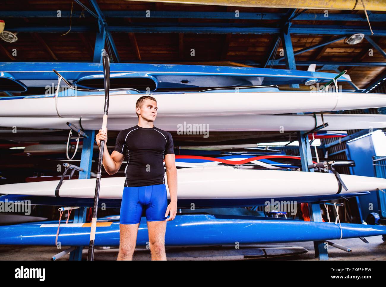 Portrat of young canoeist standing in front of stacked canoes. Concept ...
